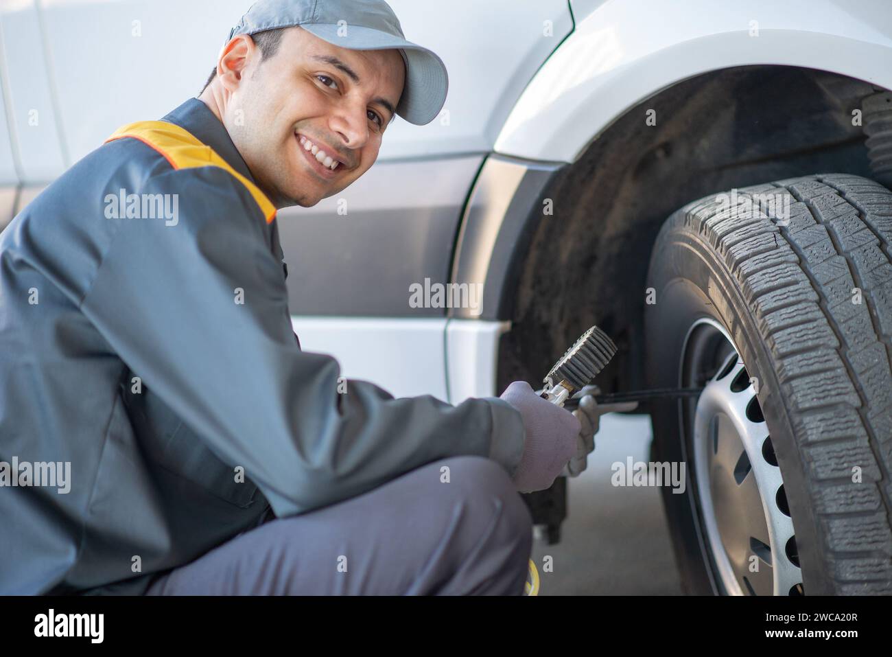 Smiling mechanic checking the pressure of a van tire Stock Photo - Alamy