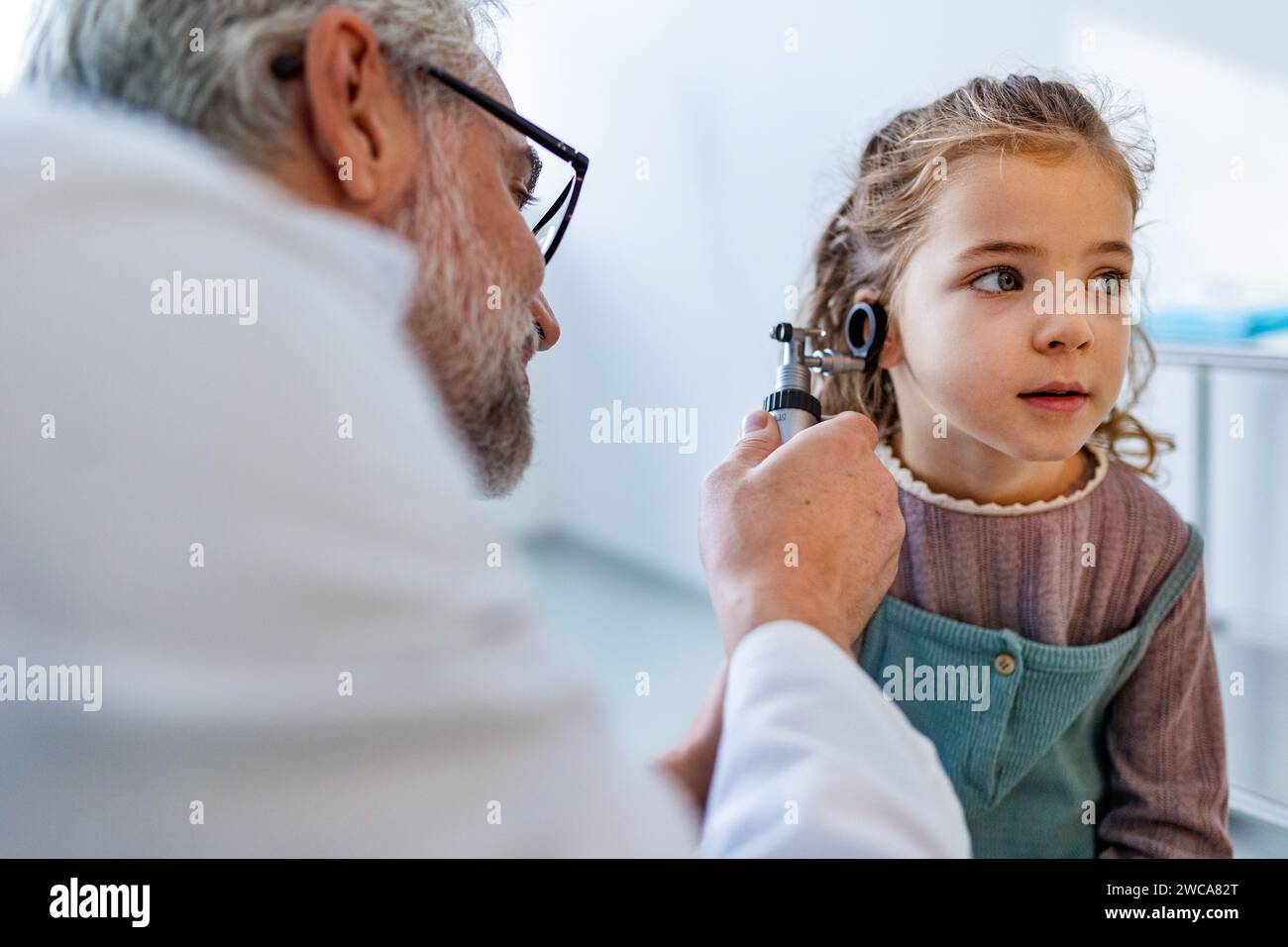 Doctor examining little girl's ear using otoscope, looking for ...