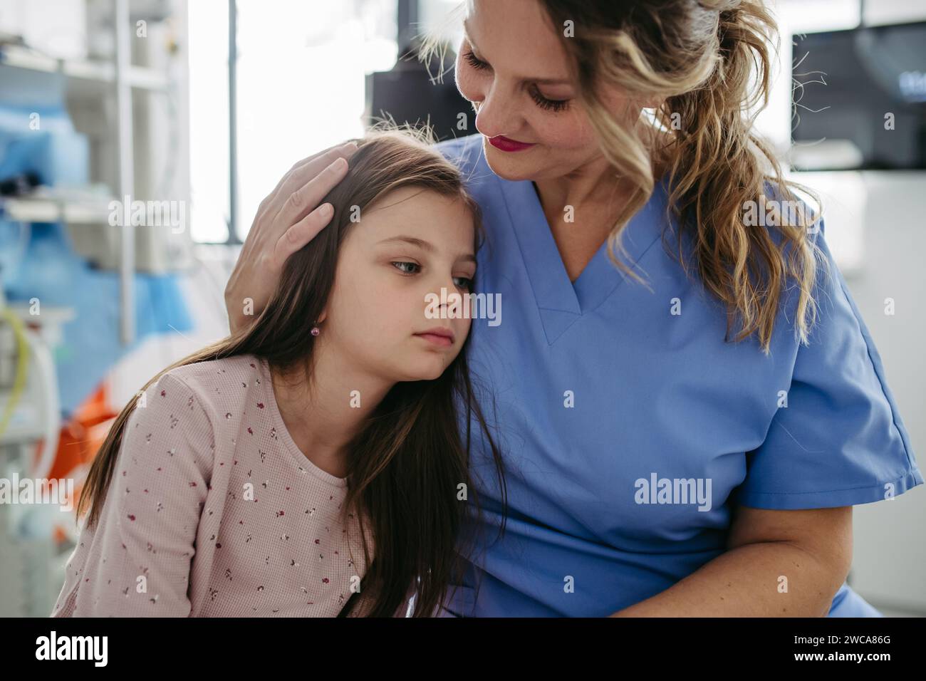 Supportive doctor soothing a worried children patient in emergency room. Hugging little girl ...