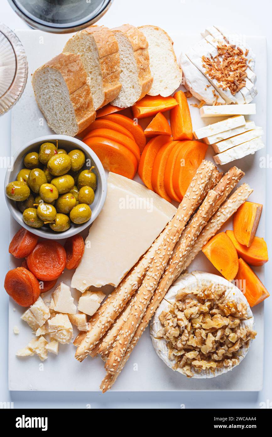 Cheese platter with persimmons, olives and wine on a white marble board ...