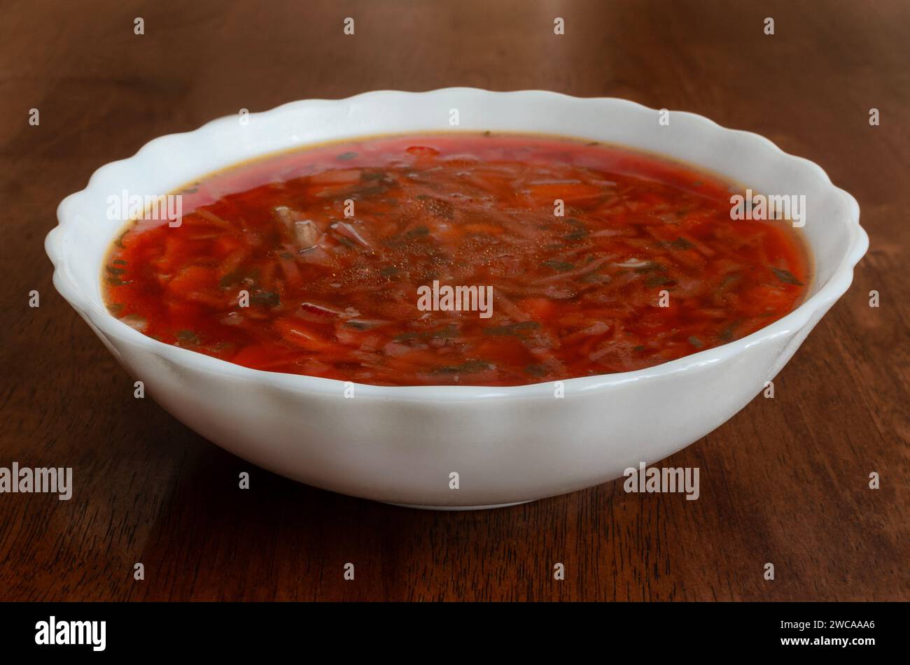 The image shows a white ceramic bowl of tomato soup placed on a wooden ...