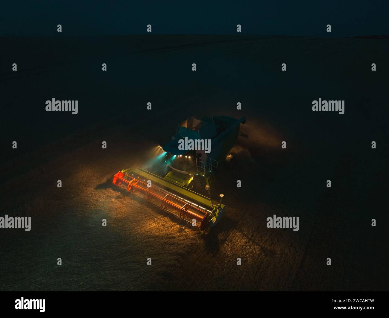 Aerial view of a tractor and harvester working in a field during night ...