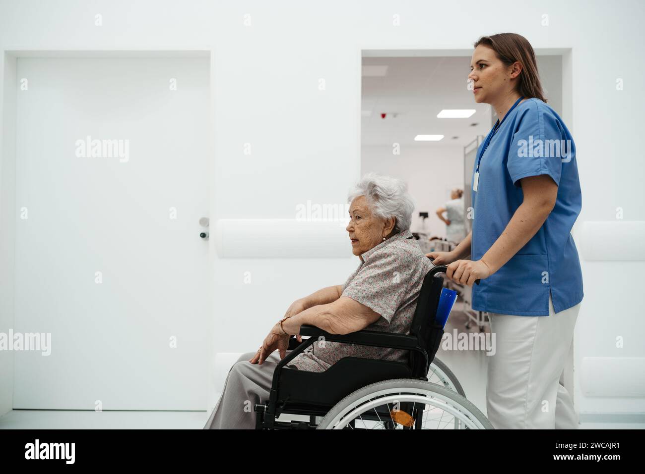 Portrait of nurse pushing senior patient in wheelchair across hospital ...