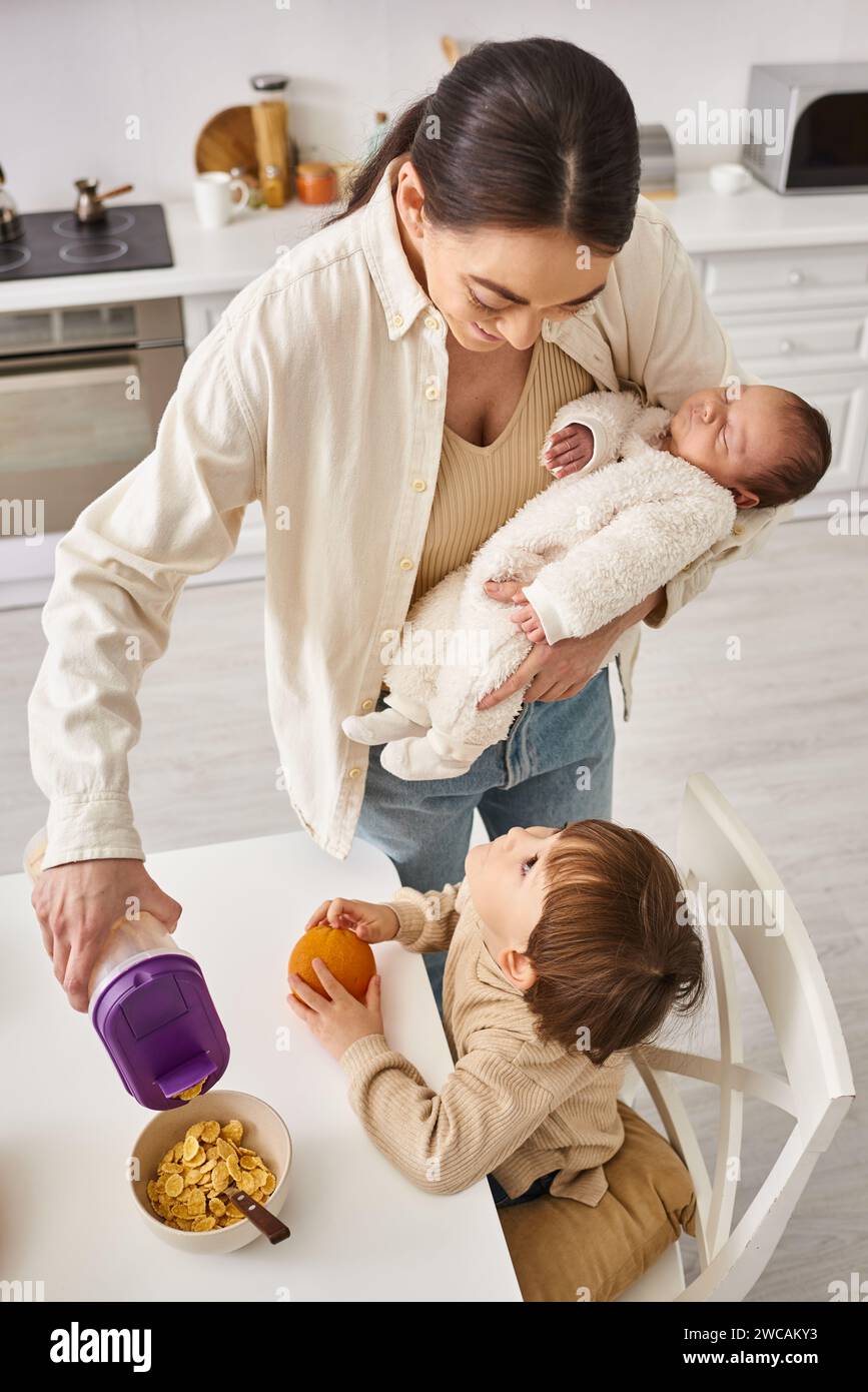 merry beautiful woman pouring corn flakes to her adorable toddler son ...