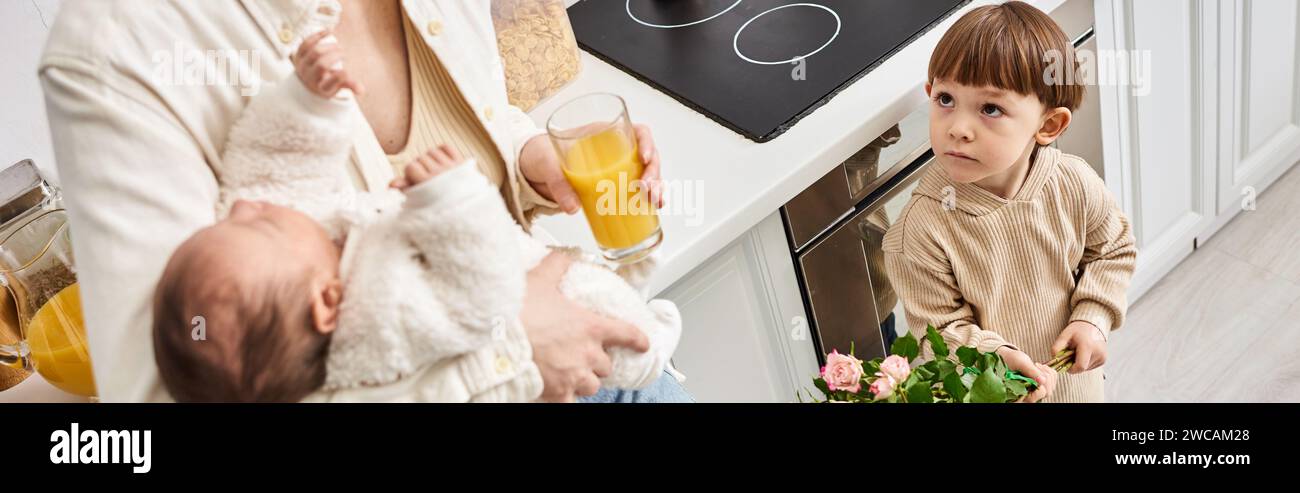 cute toddler boy giving flowers to his jolly mother with his newborn ...