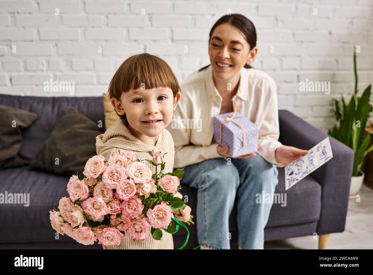 adorable toddler boy giving his mom present and postcard with flower ...