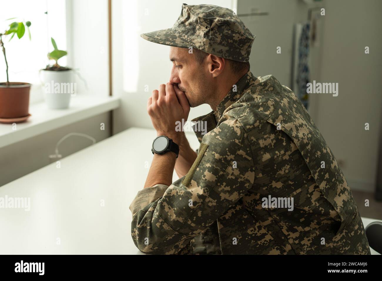 Thoughtful military man staring aside, holding palms by mouth, sitting ...