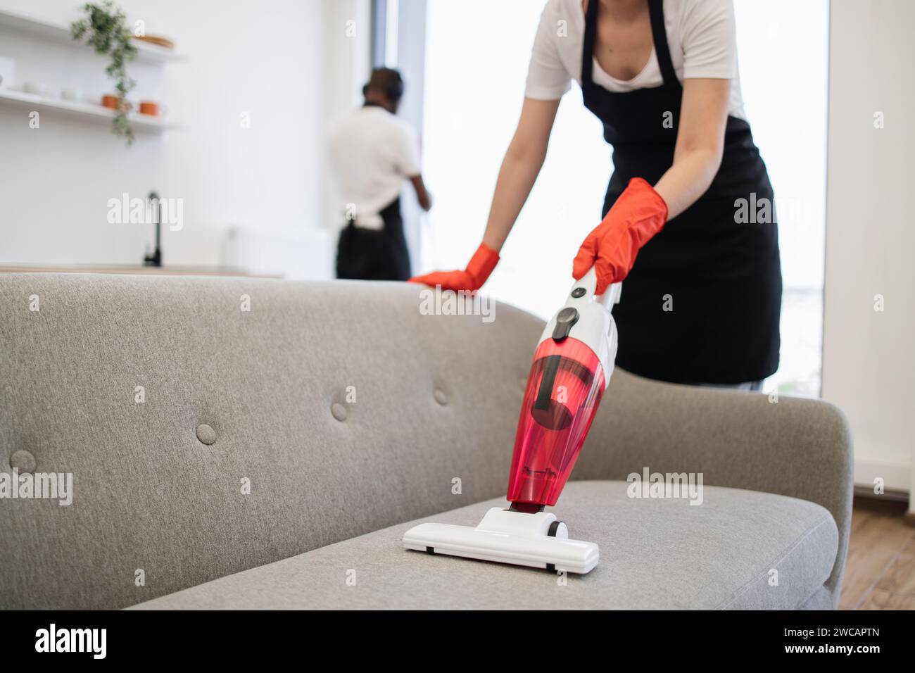 Cropped view of hands of multiethnic young female cleaner vacuuming ...