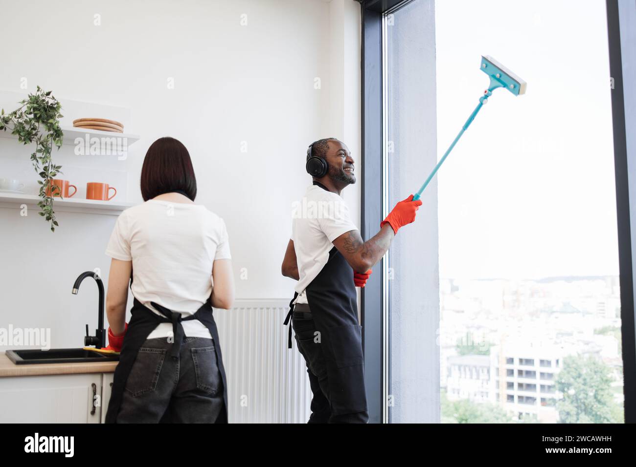 African washing windows with mop, listening to music in headphones and ...