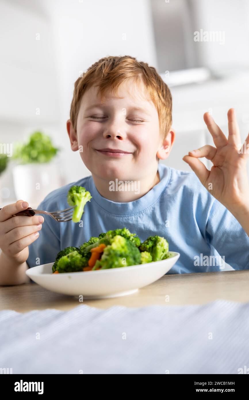A cute little boy is eating broccoli for lunch and he likes it very ...