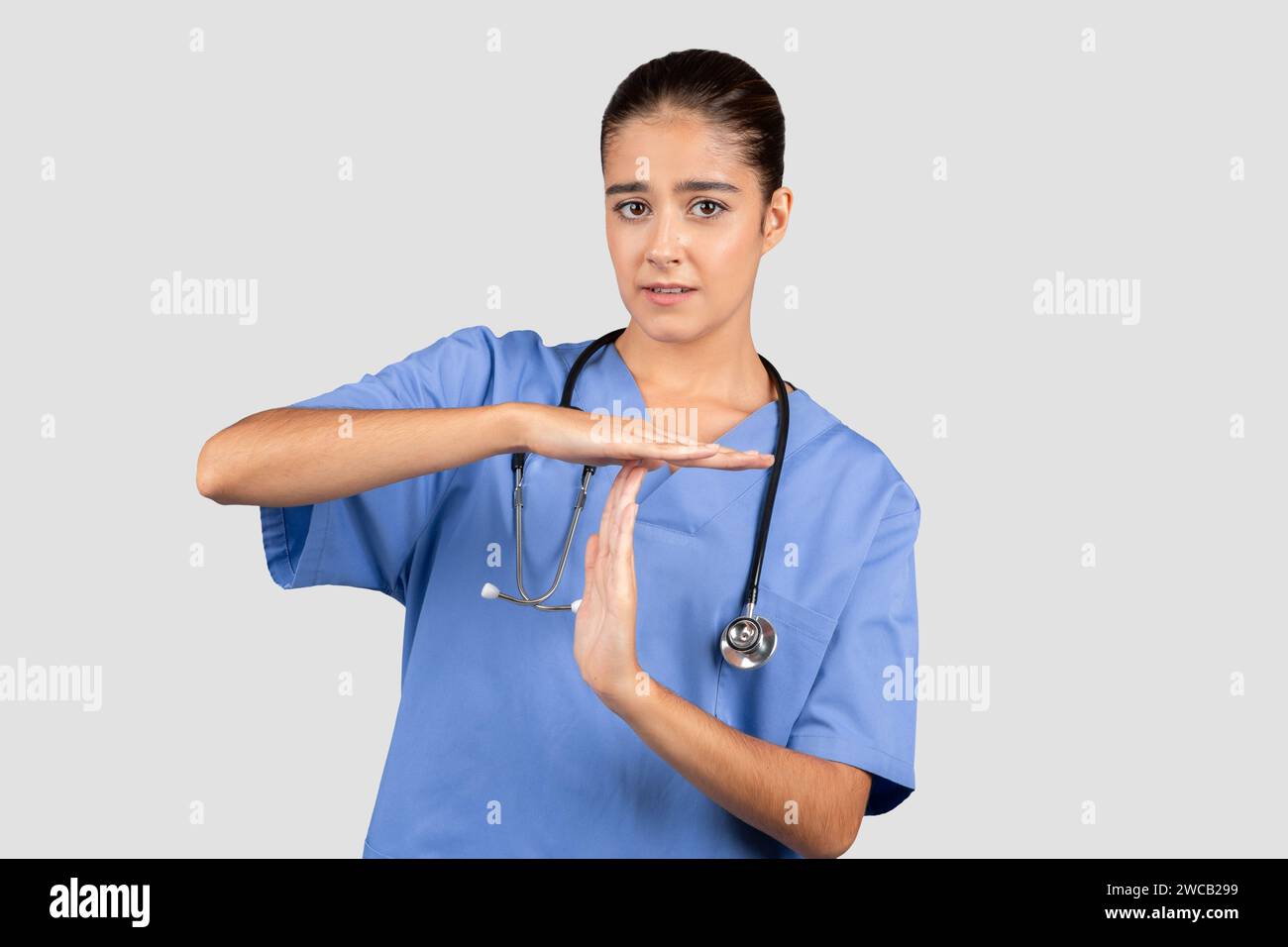 Concerned european nurse in blue scrubs making a timeout sign with her ...