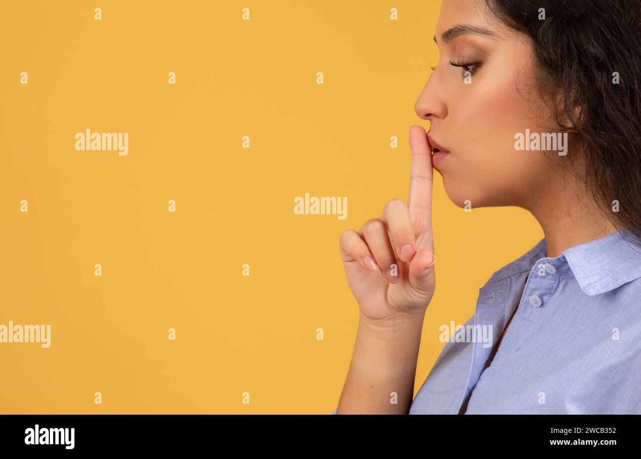 Side profile of a young woman with curly hair placing her index finger ...