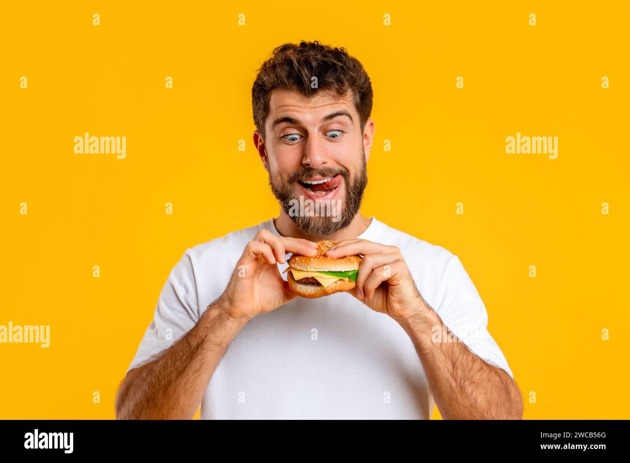 Joyful Hungry Young Guy Eating Burger Posing On Yellow Background Stock ...
