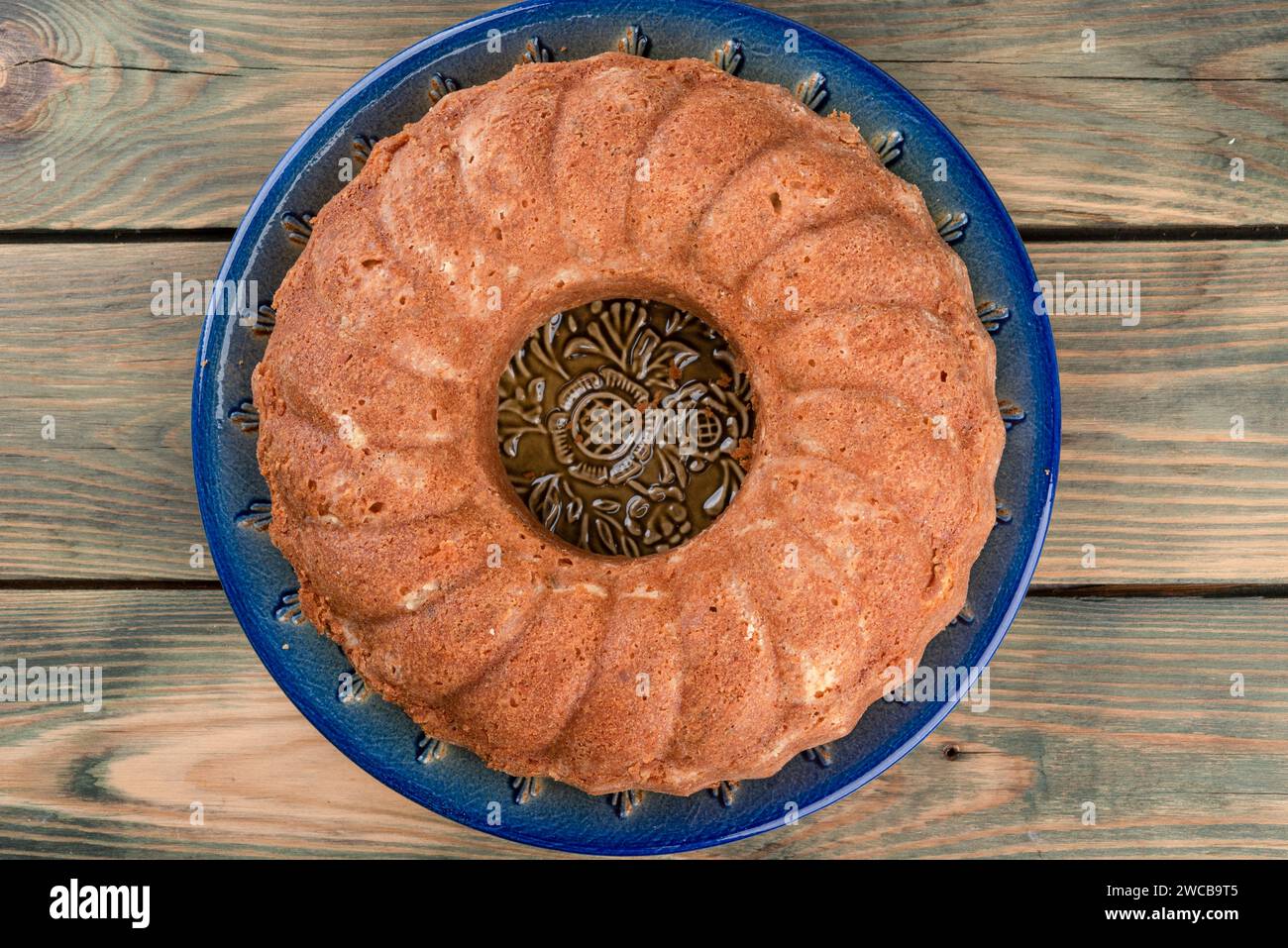 Baked round cake before frosting on a blue platter. Wooden background ...