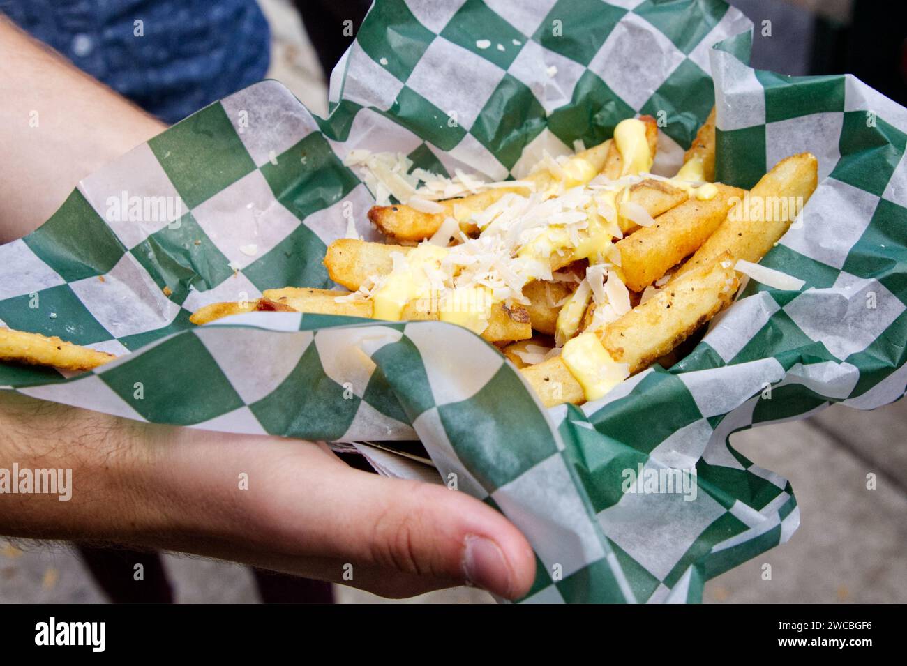 A foodie holds gourmet cheese topped French fries purchased at a food ...