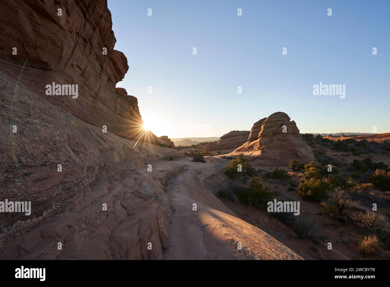 The sun peaks out behind a towering rock formation. A trail winds ...