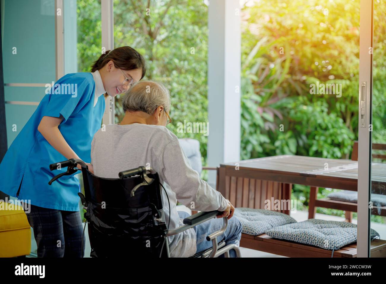 nurse is supporting elderly man sitting in wheelchair walking to looking out window Stock Photo ...