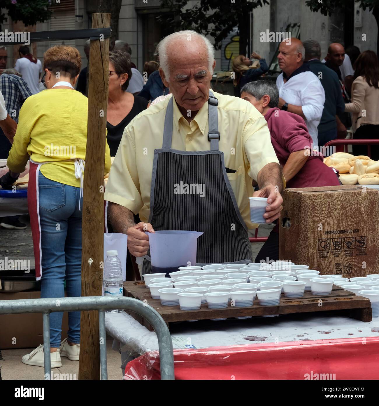senior man pours wine into cups at a stall, fiesta San Mateo, wine ...
