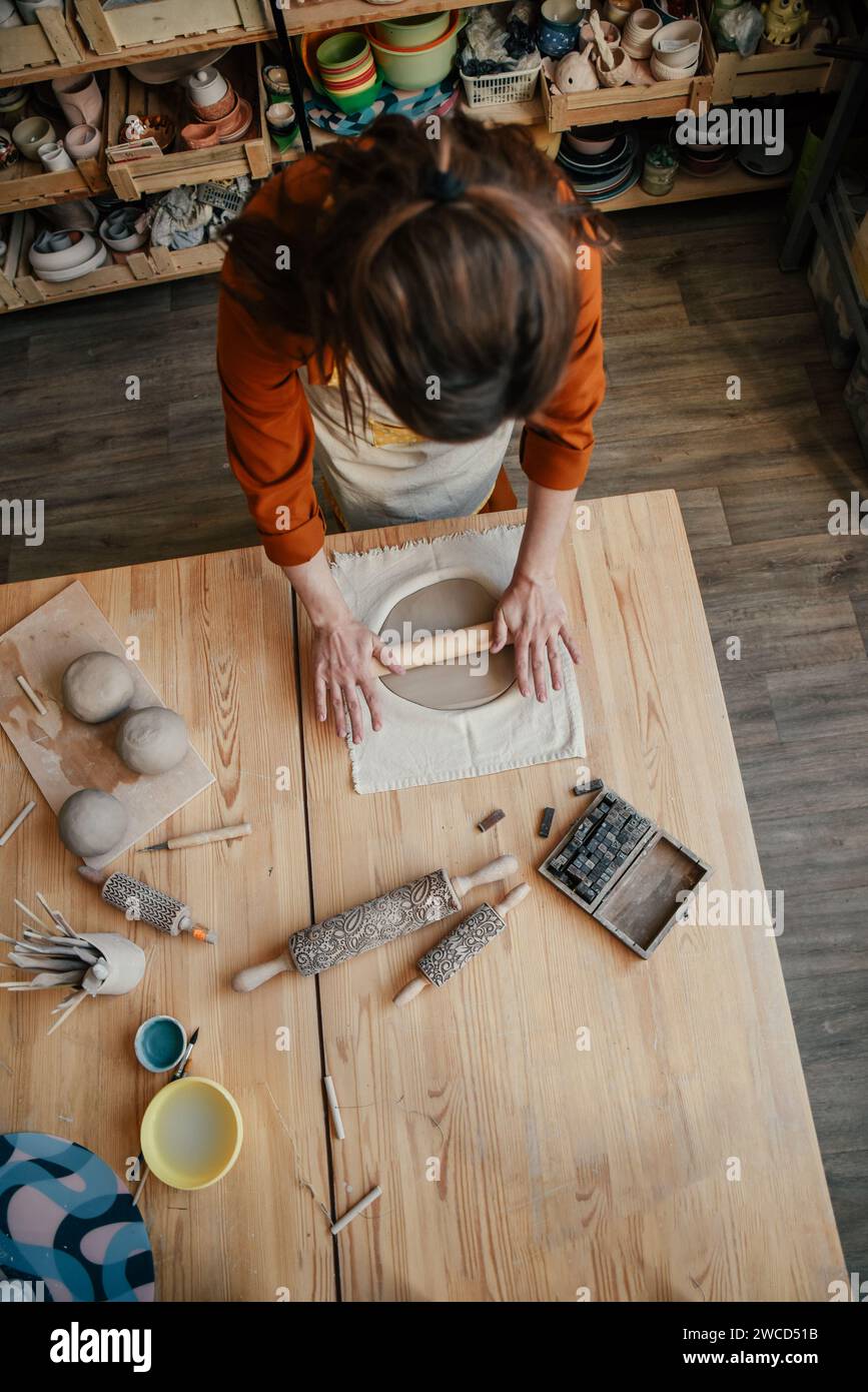 Artisan woman in lighted pottery studio, rolling clay for modelling ...