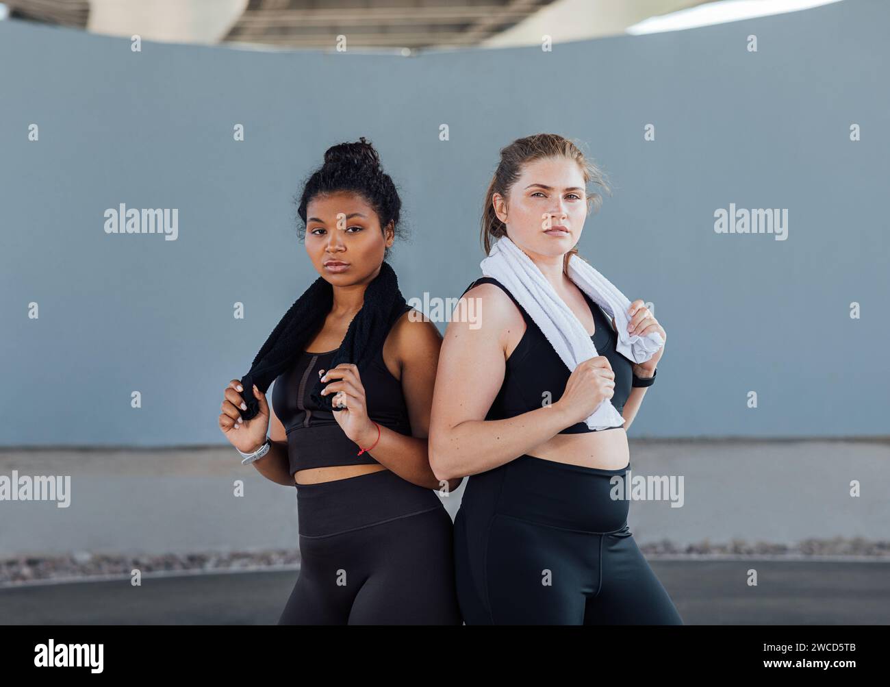 Two plus-size women in fitness wear standing back to back looking at ...