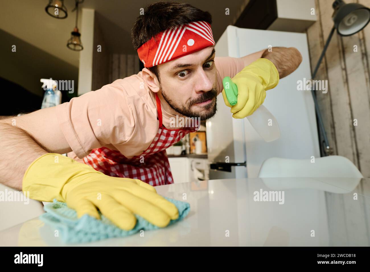 Guy in apron, headband and rubber gloves wiping table with duster and ...