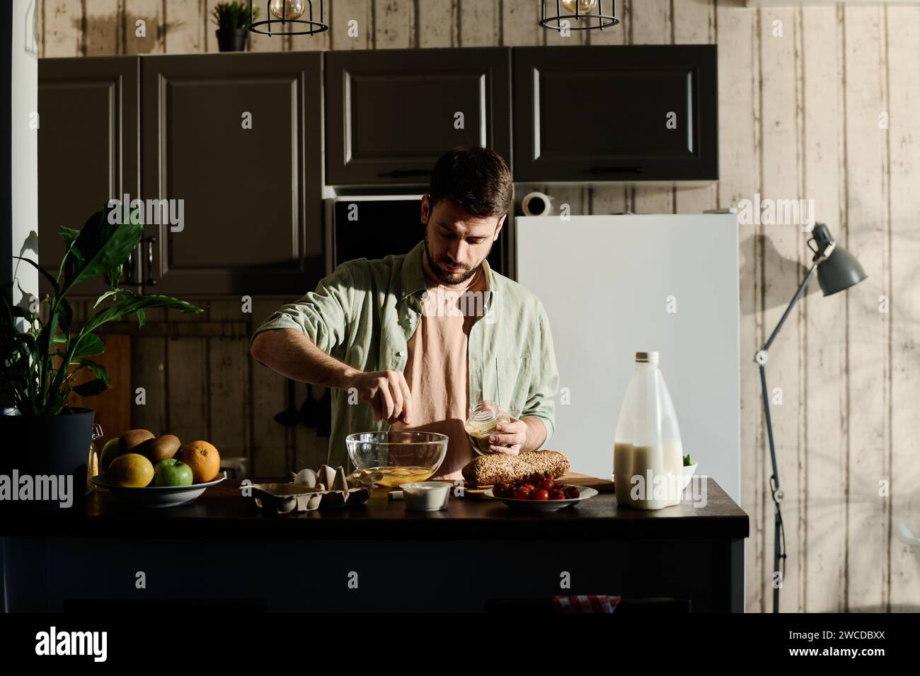 Young man putting salt into glass bowl with broken fresh raw eggs while ...