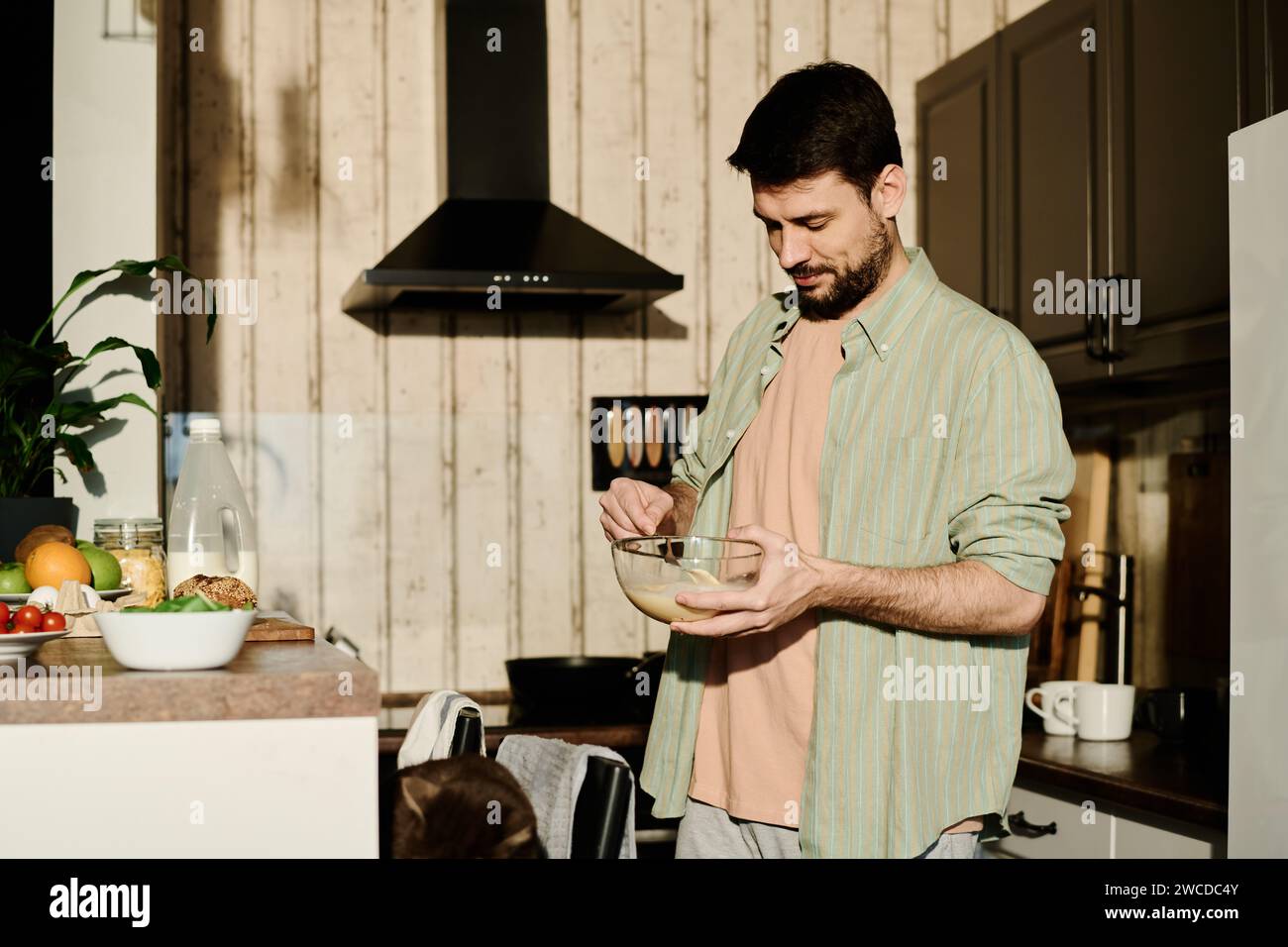 Guy in shirt standing against kitchen counter and beating raw eggs with ...