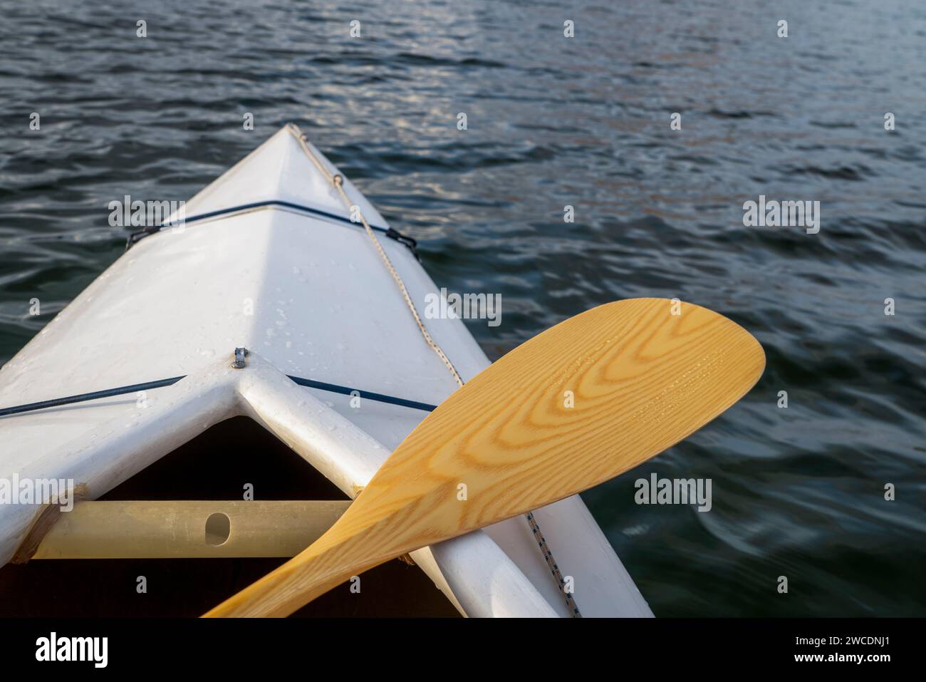 bow of a decked expedition canoe with wooden paddle on a lake, paddler ...