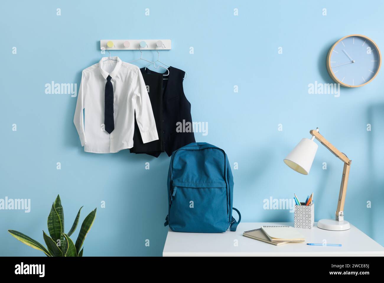 Desk with backpack, clock and stylish school uniform hanging on blue ...