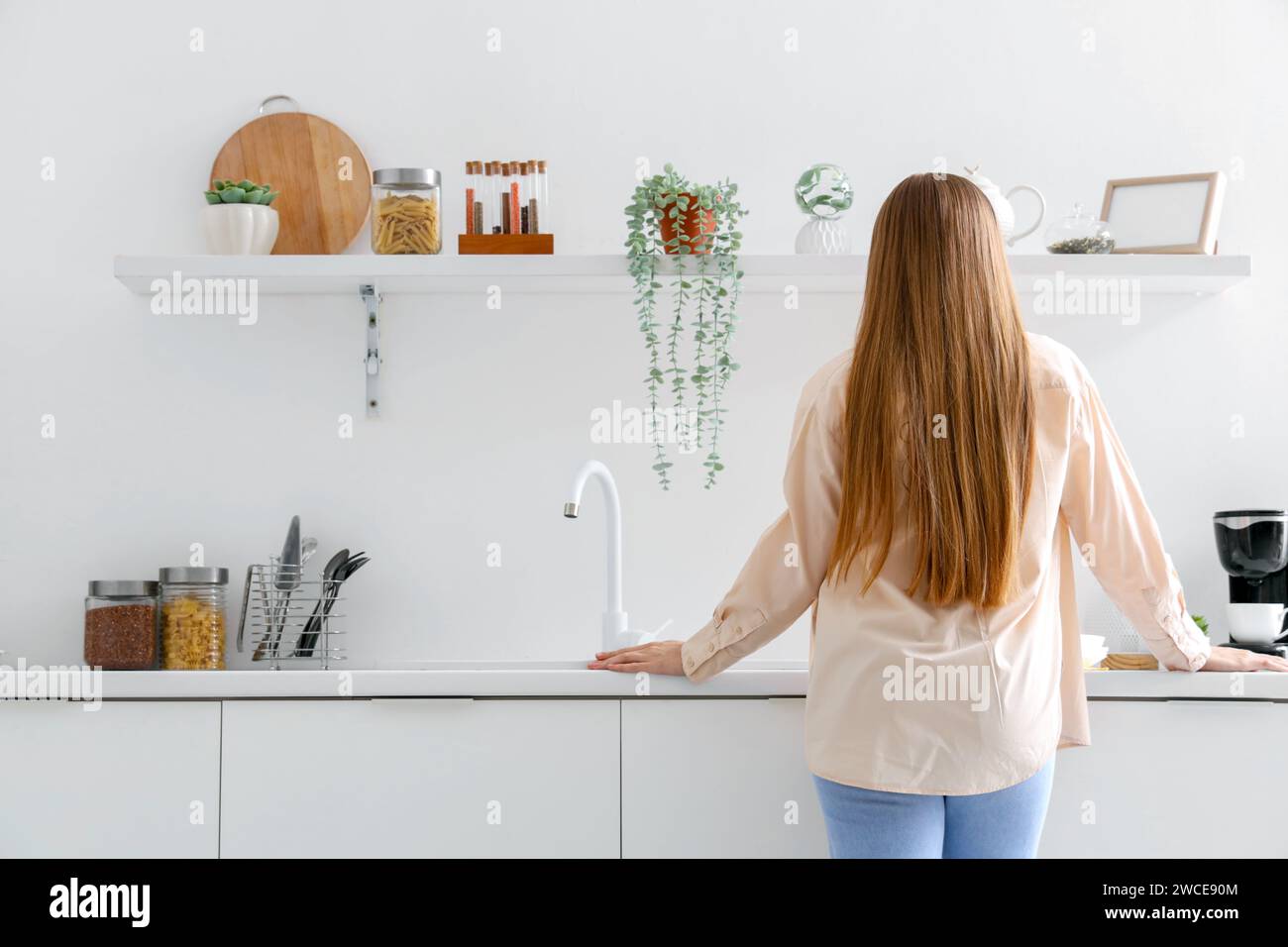 Back view of young woman standing near white counters in modern kitchen ...
