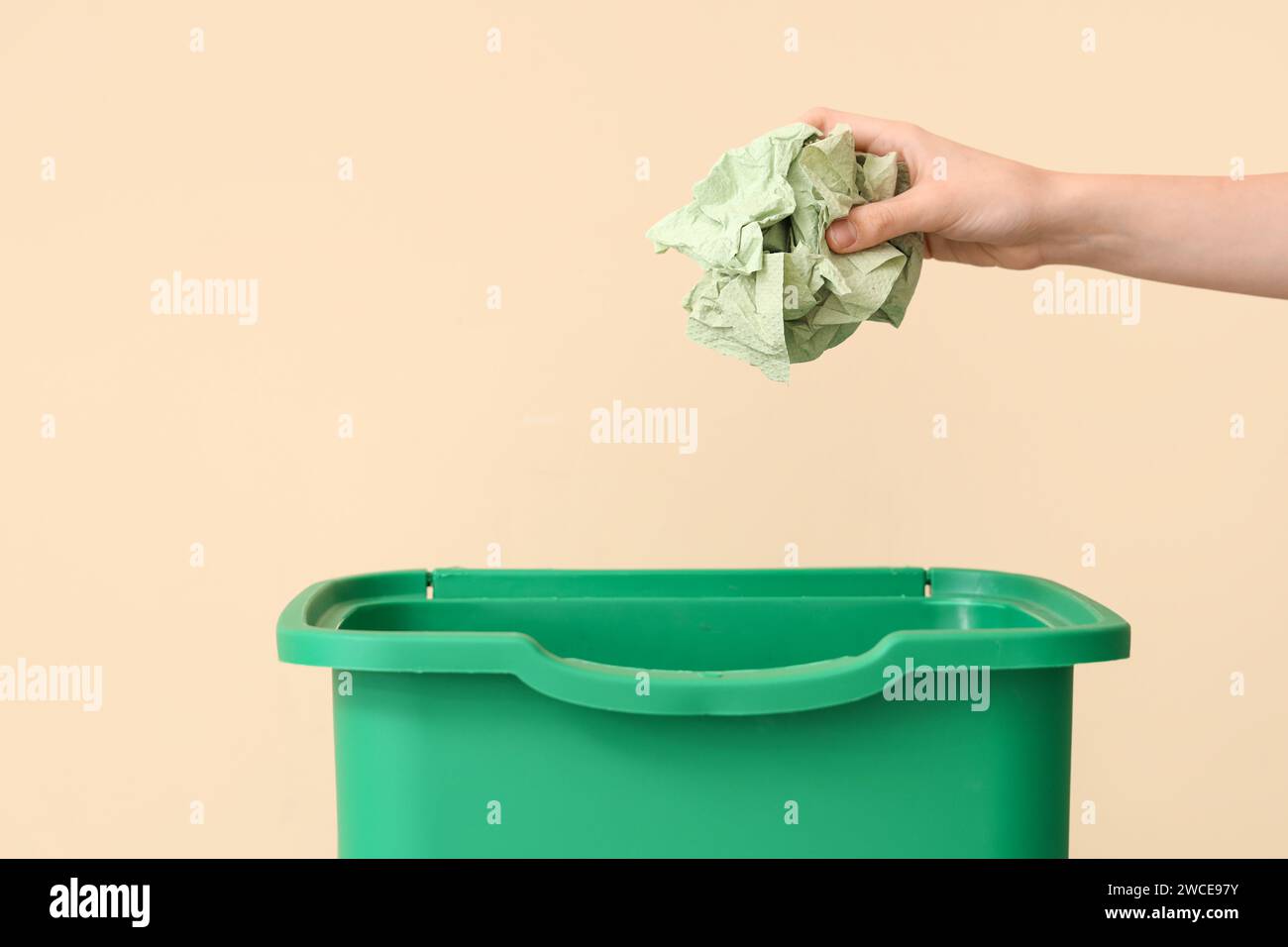 Female hand throwing crumpled paper into trash bin near beige wall ...