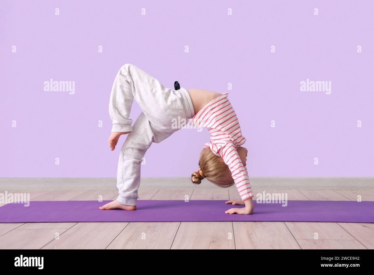 Cute little girl practicing yoga on mat against lilac background Stock ...