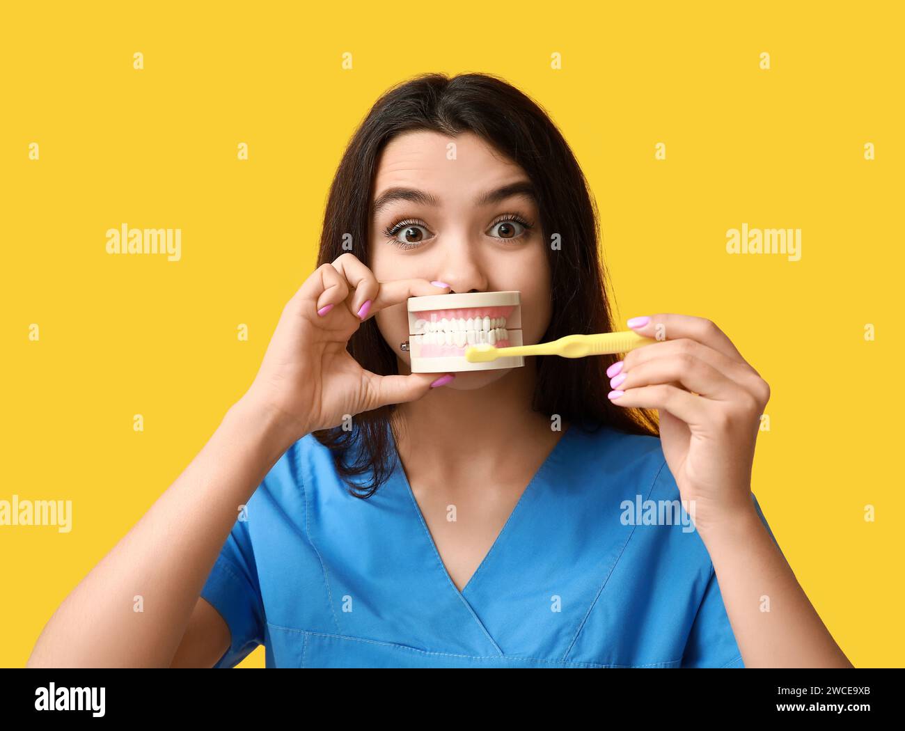 Female dentist with jaw model and toothbrush on yellow background ...