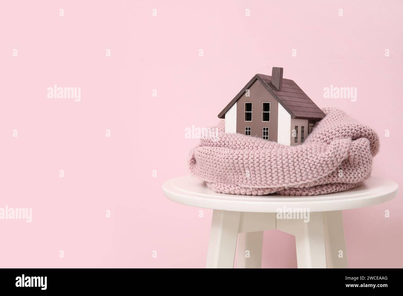Decorative house with scarf on stool against pink background. Winter ...
