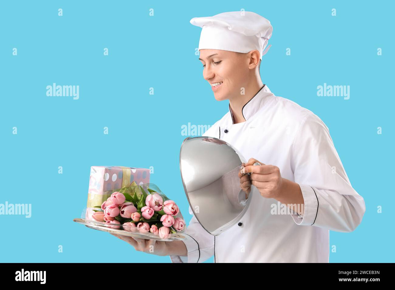 Male chef with cloche, gift and tulips on blue background ...