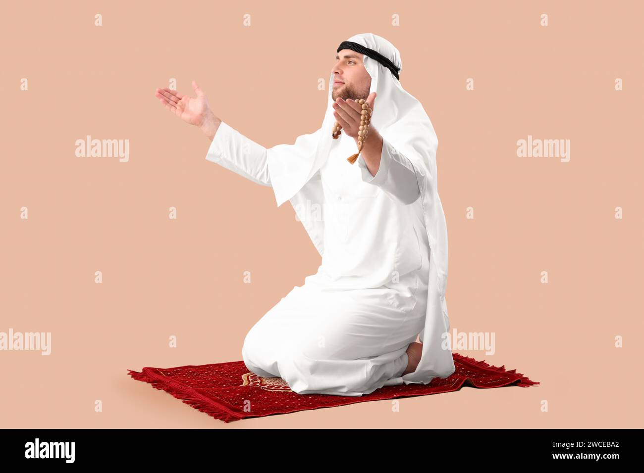 Young Muslim man praying on mat against beige background. Ramadan ...