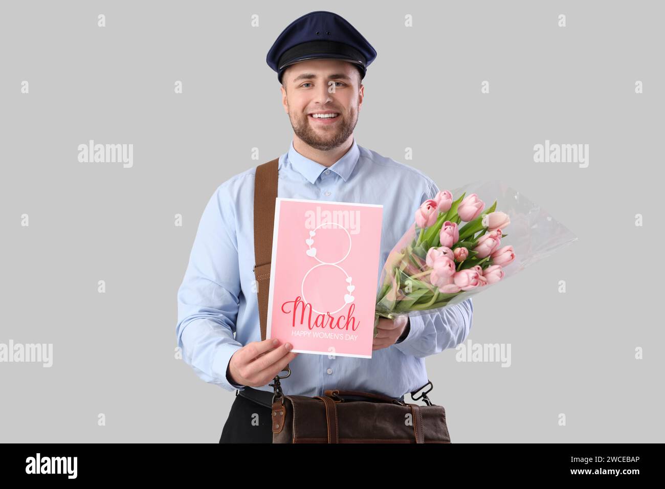 Handsome postman with tulips and greeting card on light background ...