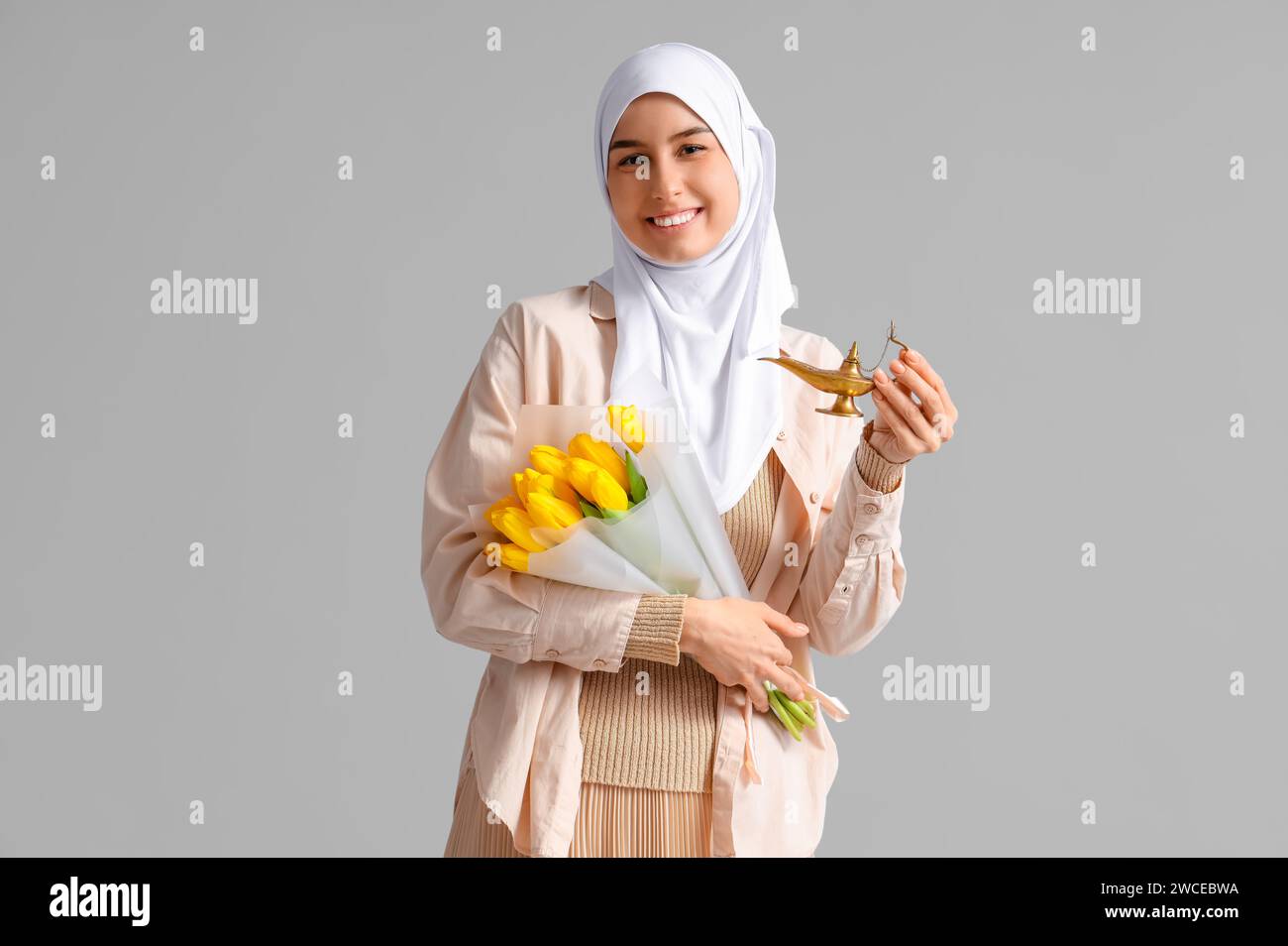 Young Muslim woman with Aladdin lamp and tulips on light background ...