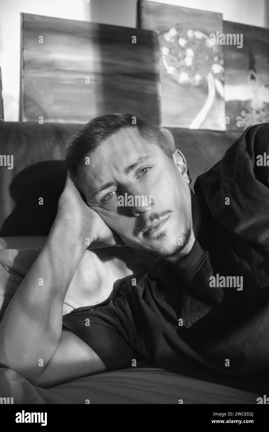 Young artist posing on bed on background of paintings. Handsome man ...