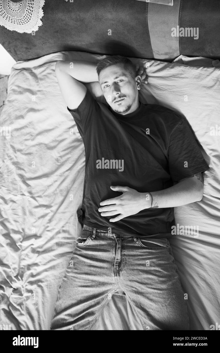 Young artist posing on bed on background of paintings. Handsome man ...