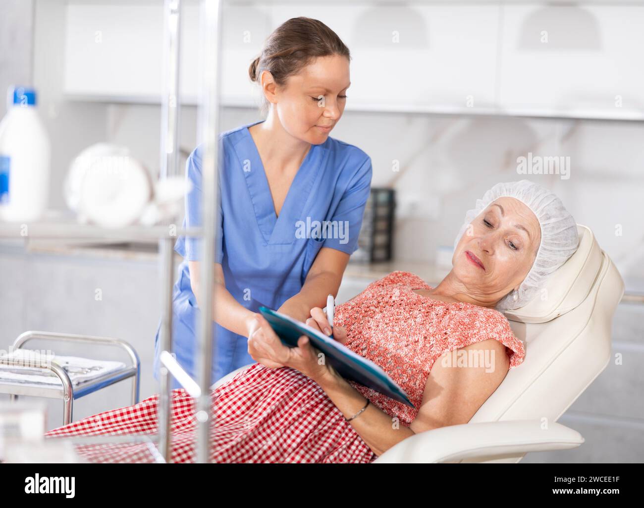 Mature woman patient sits in chair and reads documents with woman ...