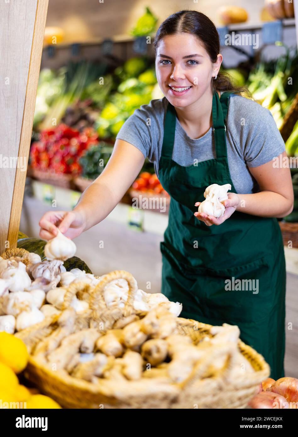Woman seller wearing apron arranges garlic and other vegetables on ...