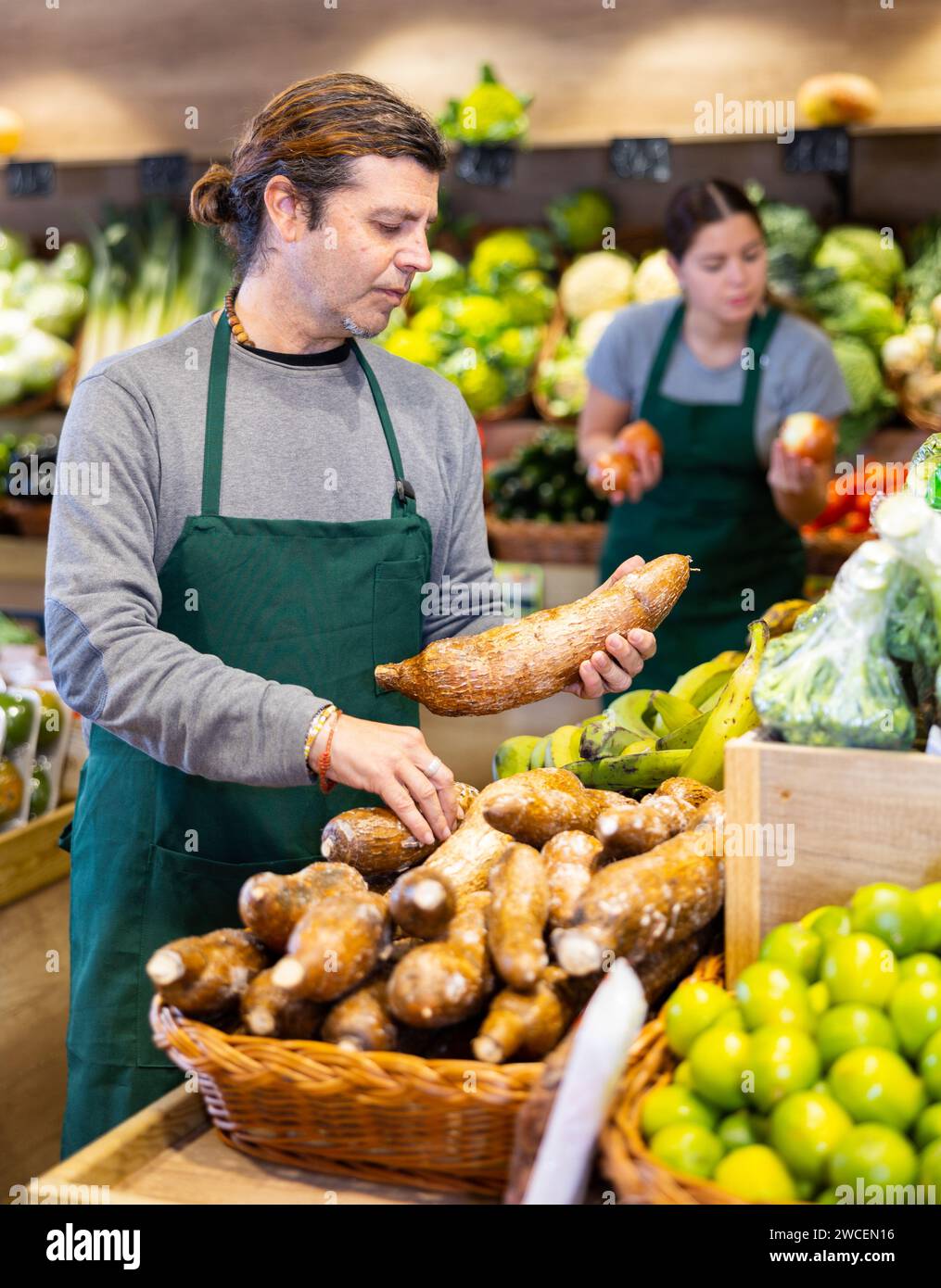 Salesman in apron offering root yucca on supermarket Stock Photo - Alamy