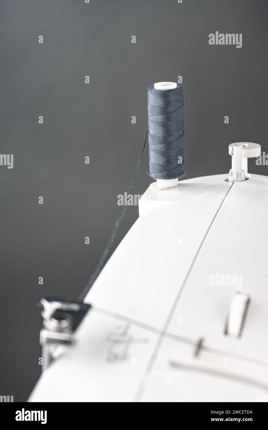 Spool of gray sewing thread stands on top of a white modern sewing ...