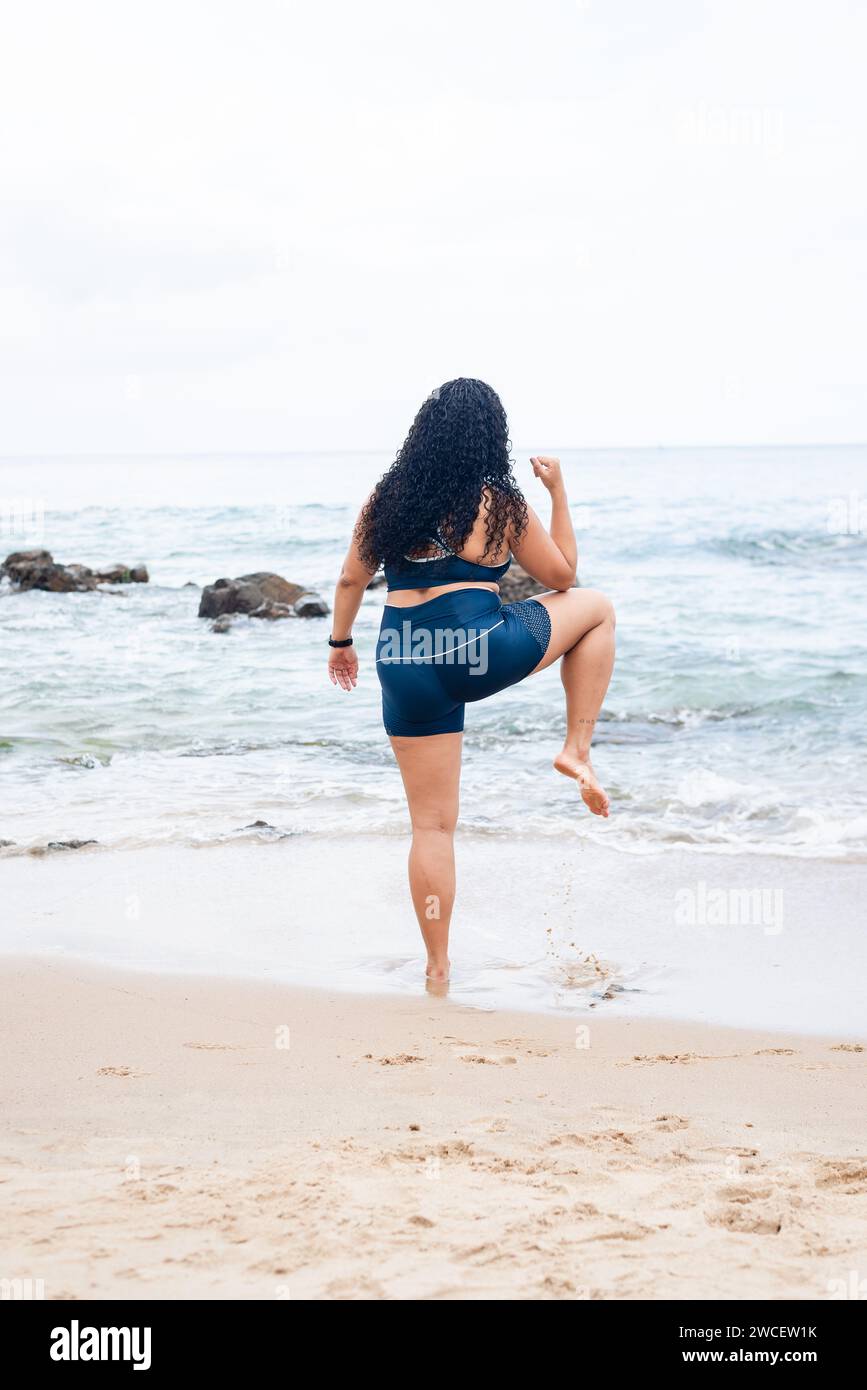 Fitness woman, standing, doing leg exercises on the beach sand with her ...