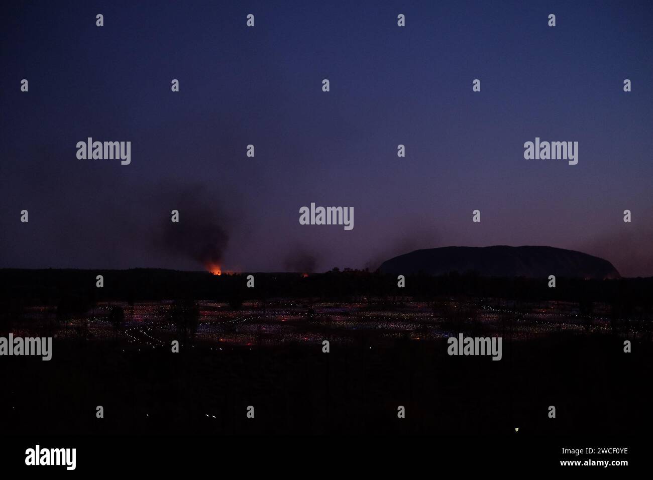 Overlooking Uluru in Central Australia, a fire glows on the horizon ...