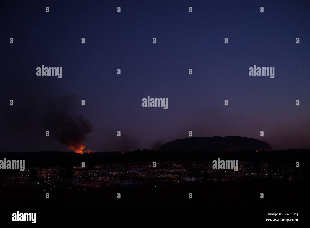 At Uluru in Central Australia a grassfire flares up on the horizon ...