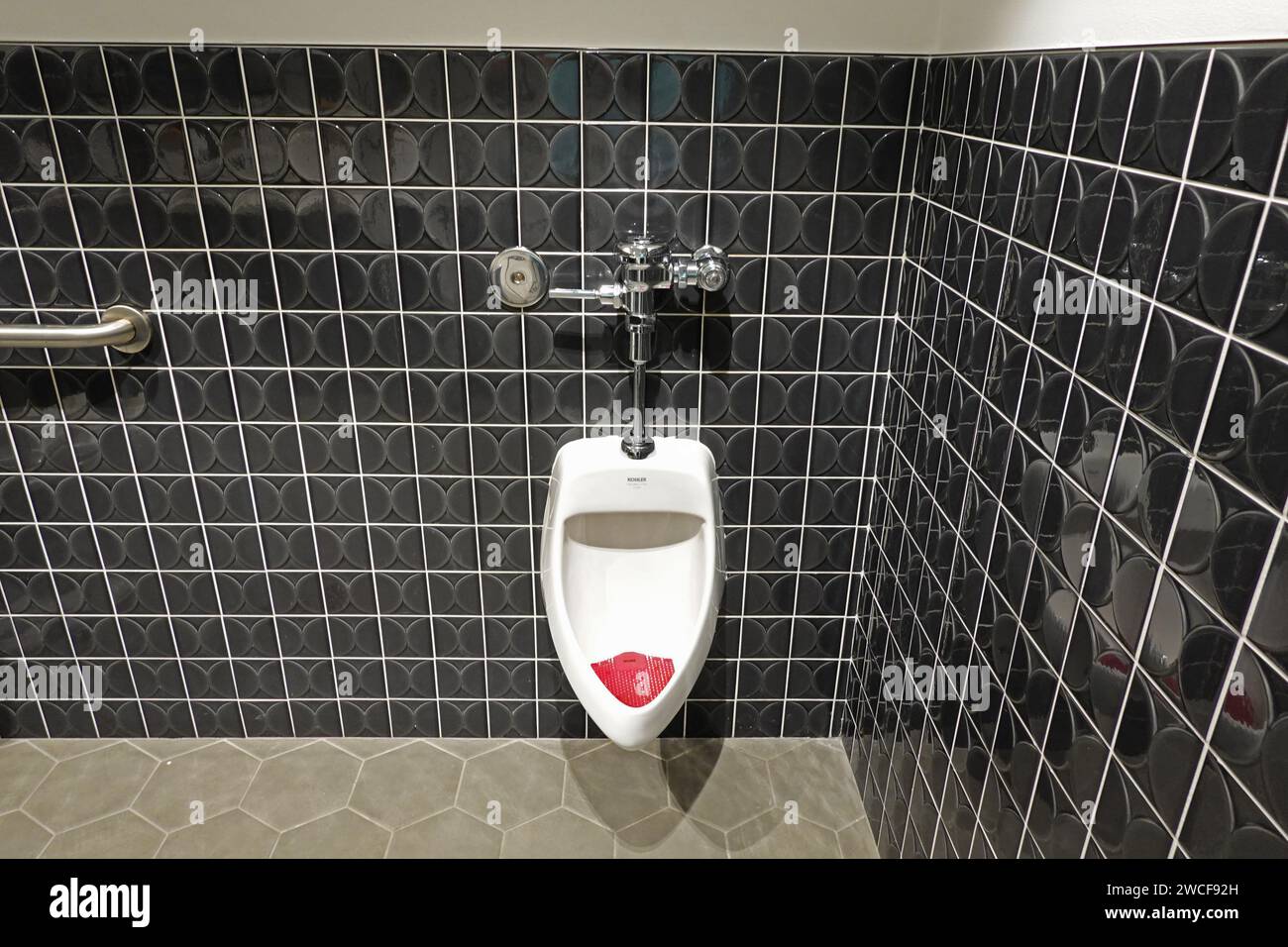 Black tiled walls and urinal inside a men's bathroom in a hair salon ...