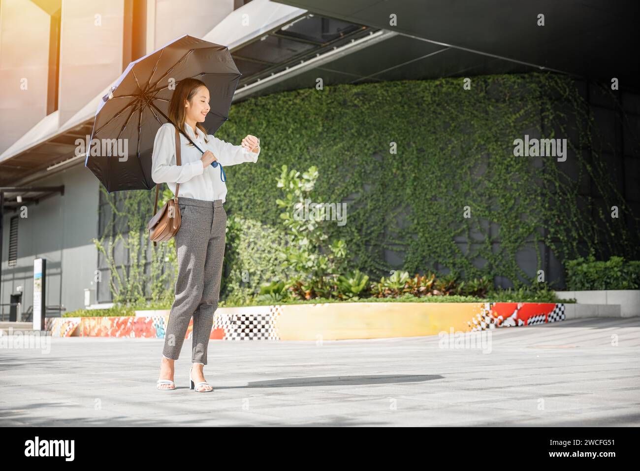 In hot weather, a young businesswoman uses an umbrella on her way to ...