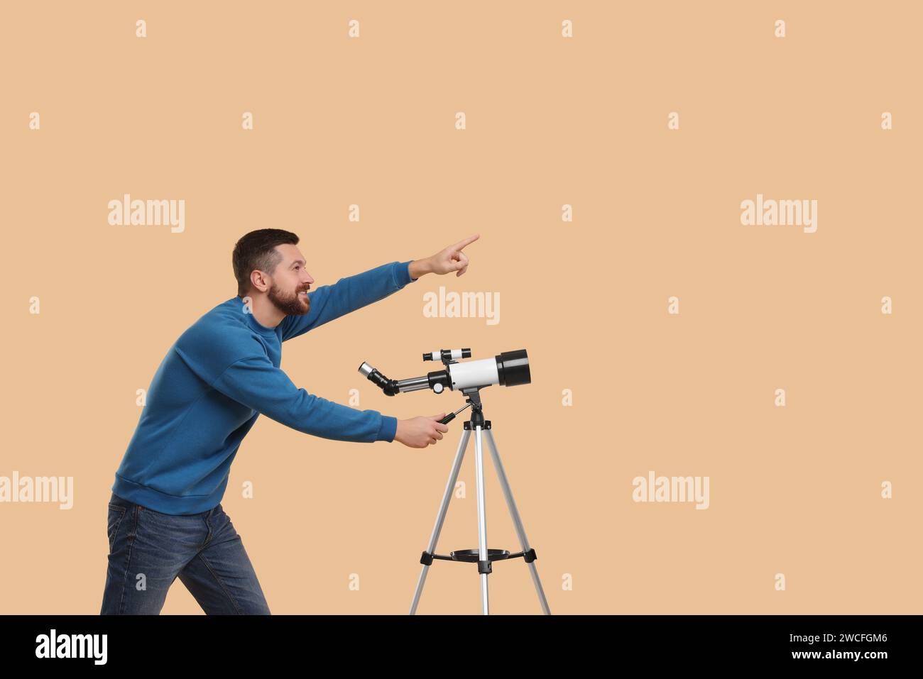 Happy astronomer with telescope pointing at something on beige ...
